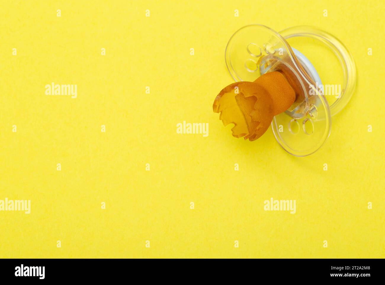 Low-quality torn baby silicone pacifier on a yellow background, close ...