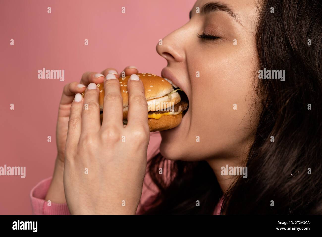 Cute young female snacking on a sandwich with her eyes closed during ...