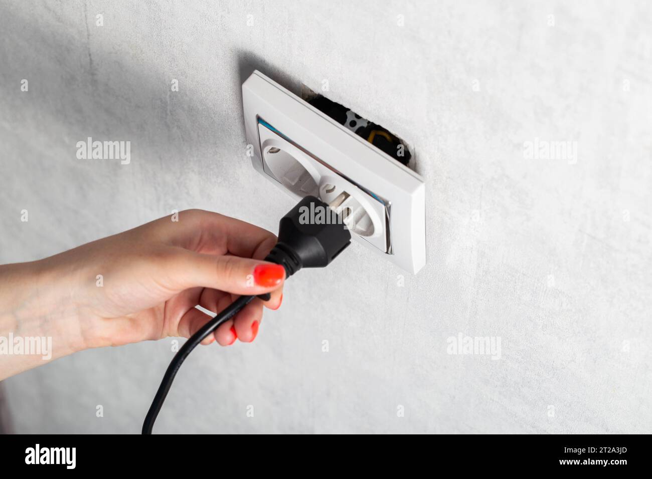 The girl puts the electric plug into a broken socket. Risk of electric ...