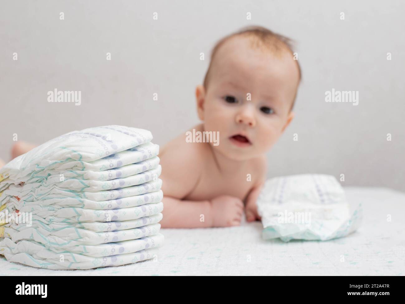 A little boy at the age of 5 months lies in a diaper on a white ...