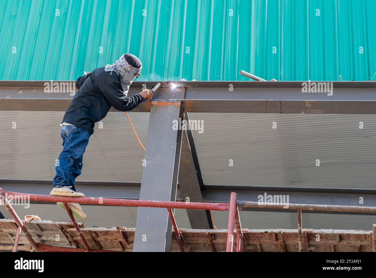 A welder is welding steel on a steel roof truss in construction site ...