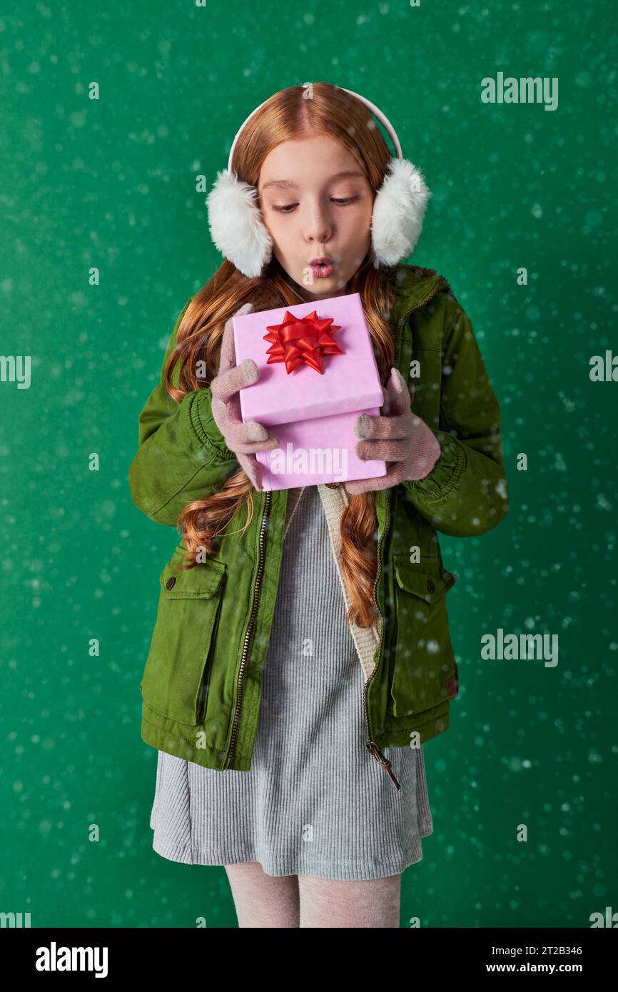 preteen girl in ear muffs, scarf and winter attire blowing snow from ...