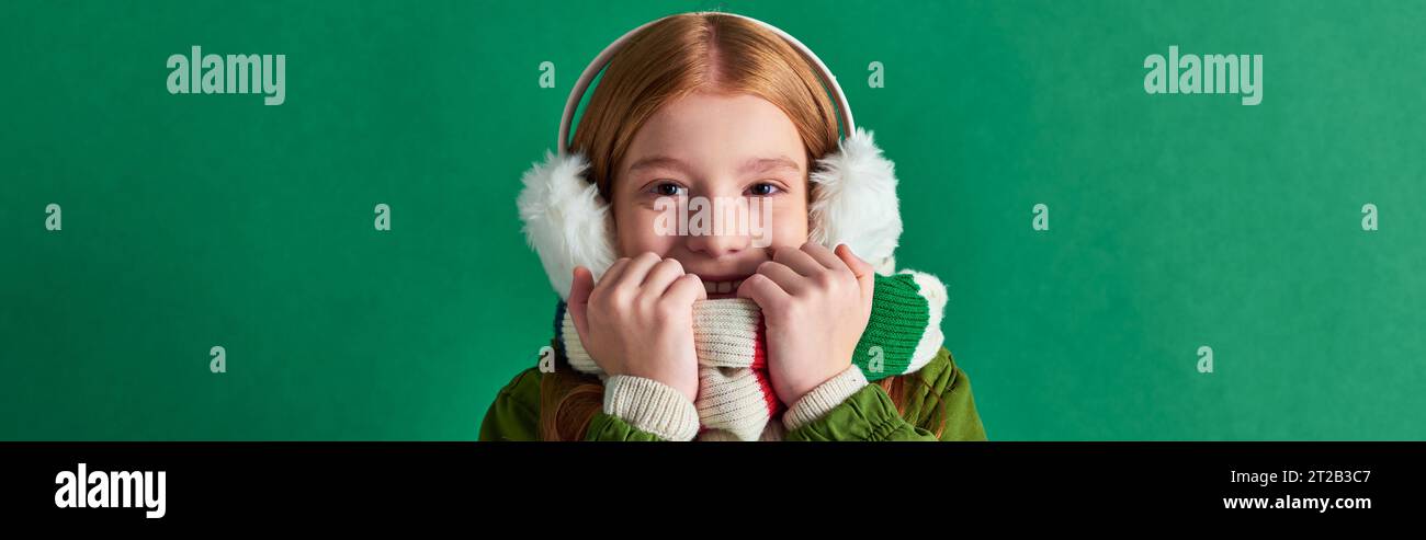 cute girl in striped scarf and winter ear muffs smiling on turquoise ...