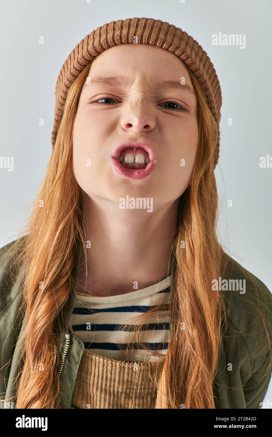 angry preteen girl in knitted hat and outerwear showing teeth and ...