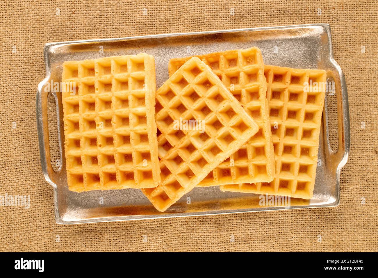 Four freshly baked aromatic waffles with metal tray on jute cloth ...