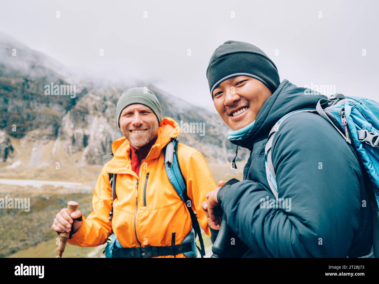 Caucasian and Sherpa men with backpacks together smiling at camera ...