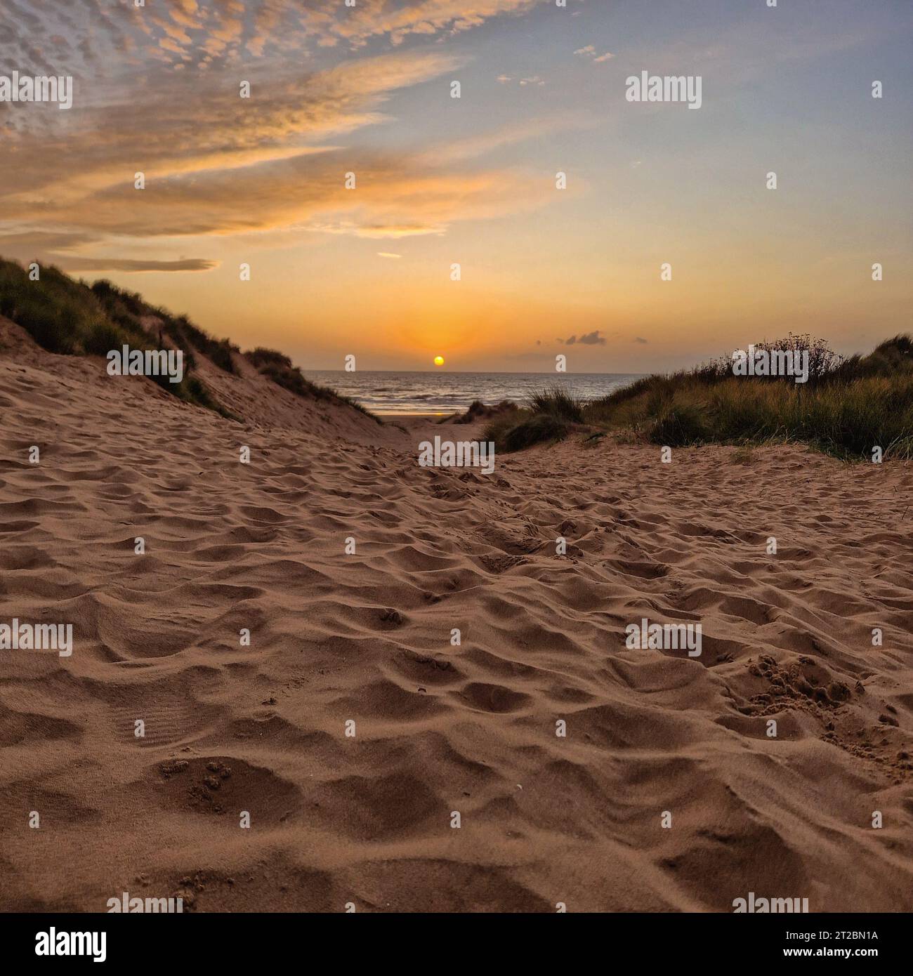 The sun dips below the horizon, casting a golden glow over Formby Beach ...