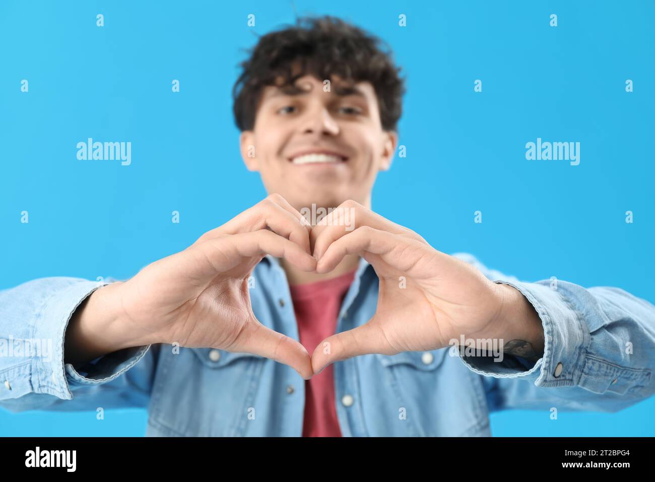 Handsome young man making heart with his hands on light blue background ...