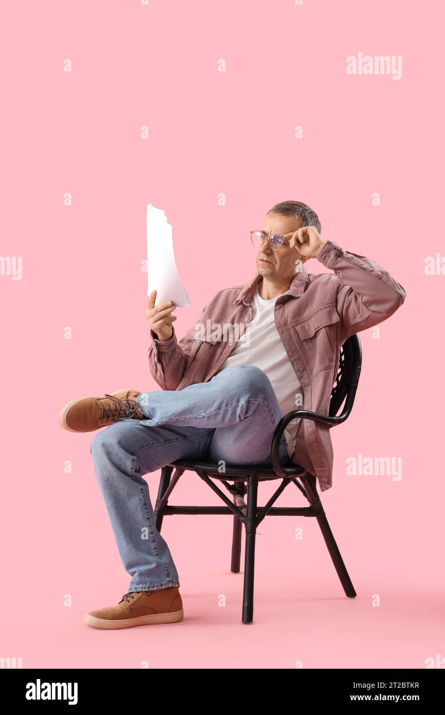 Mature actor reading film script in chair on pink background Stock ...