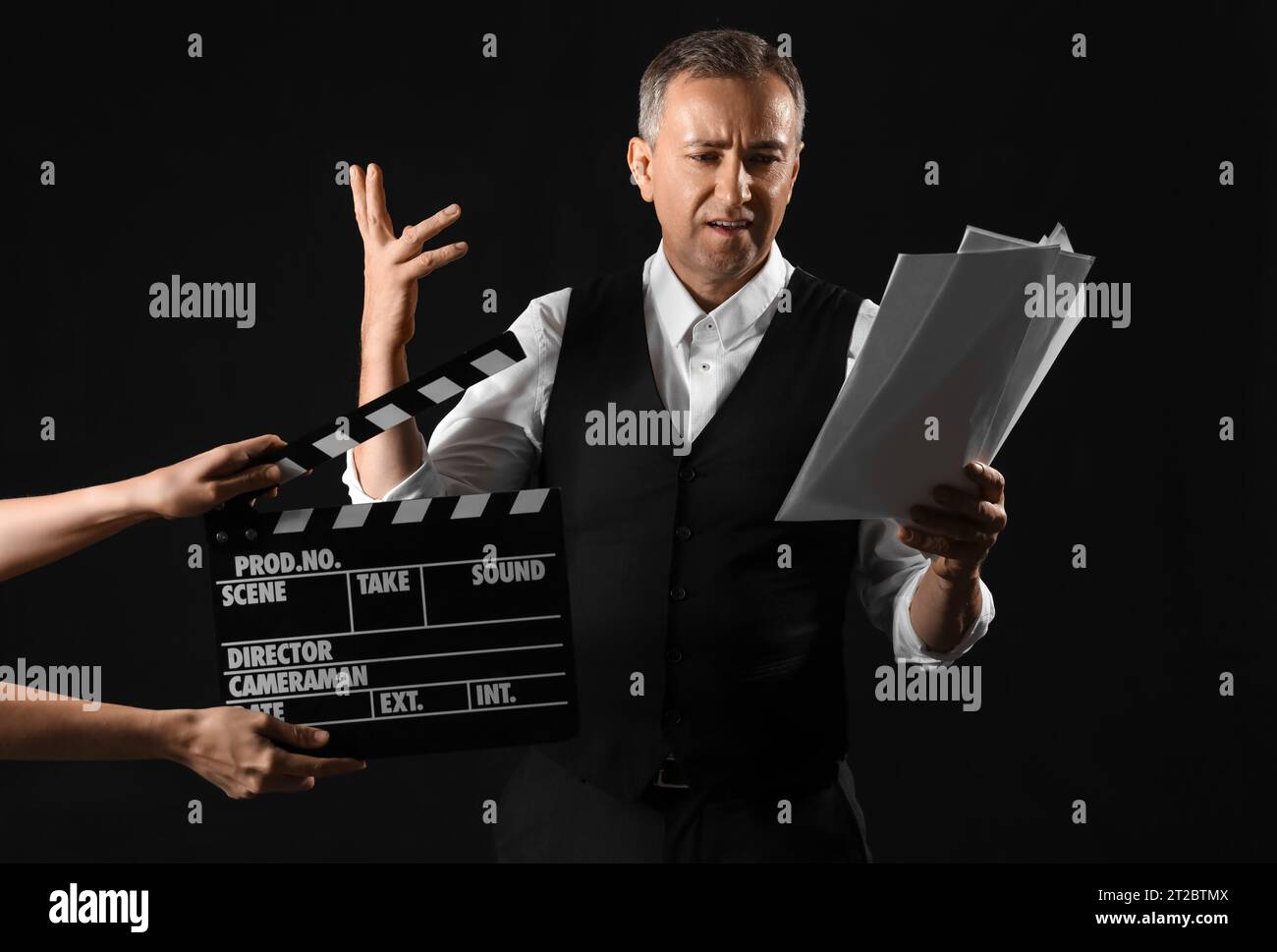 Mature actor reading script and hands with clapperboard on dark ...