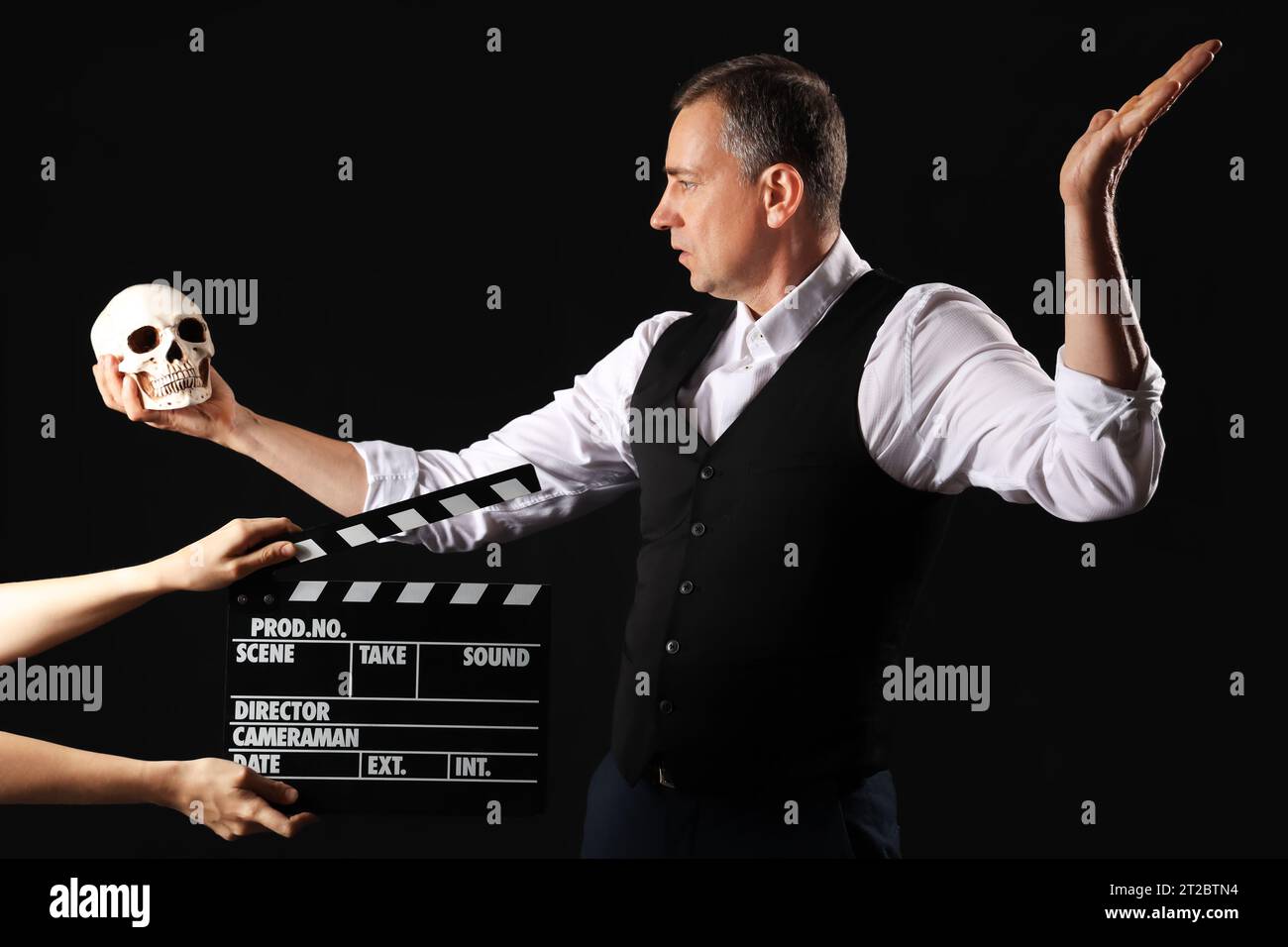 Mature actor holding skull and hands with clapperboard on dark ...