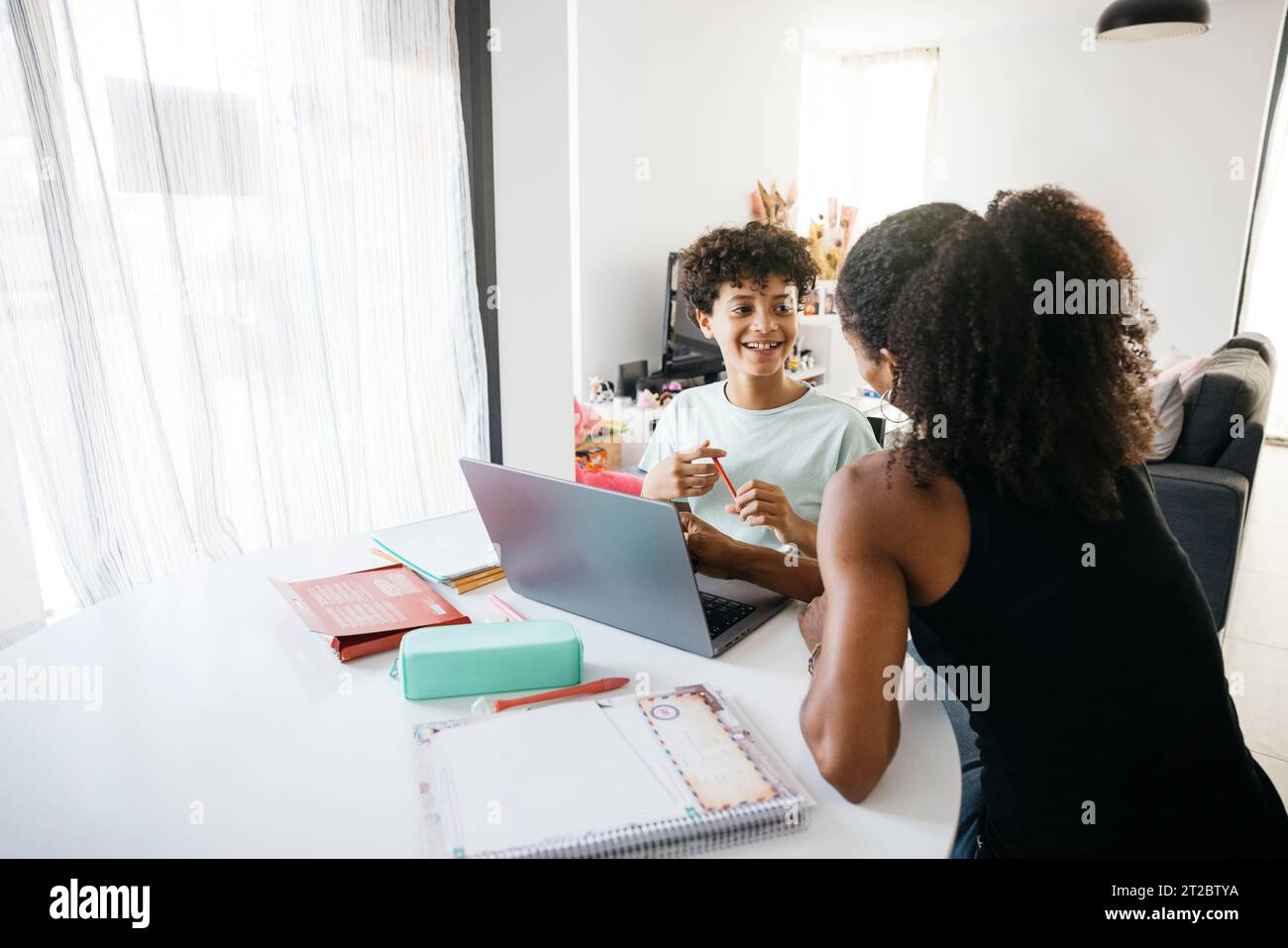 Cheerful woman helping daughter doing homework. Happy mother assisting her daughter with school ...