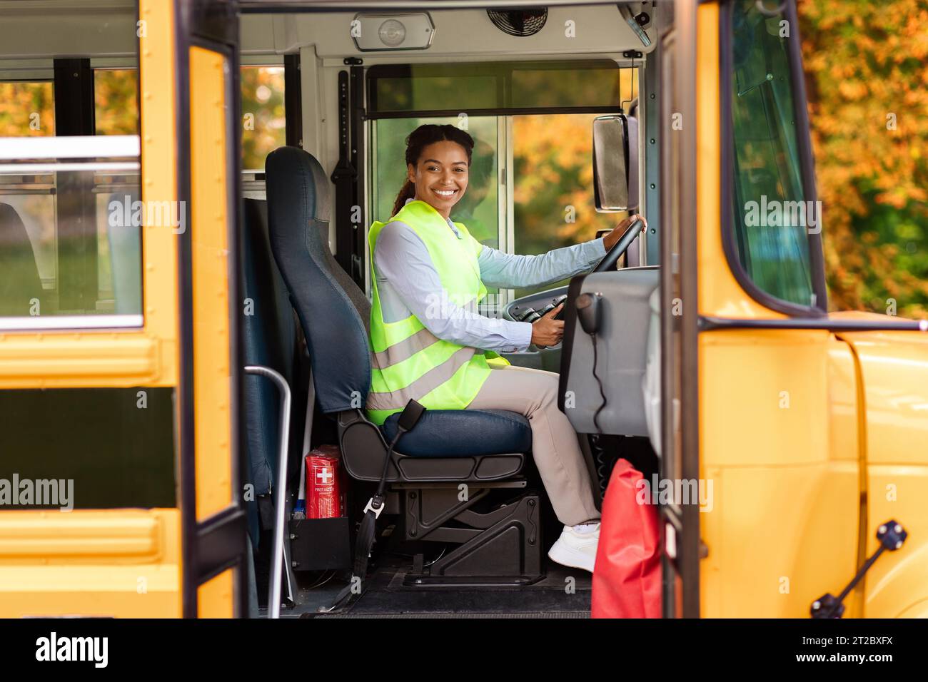 Joyful black female driver sitting in yellow school bus, smiling at ...
