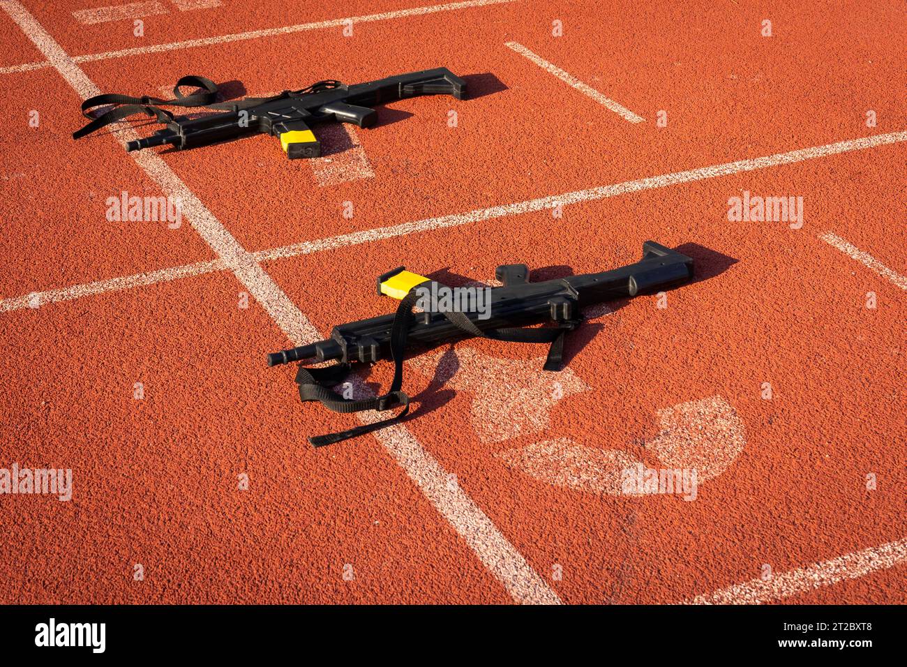 Black practice weapons on the dotted starting line of an orange running ...