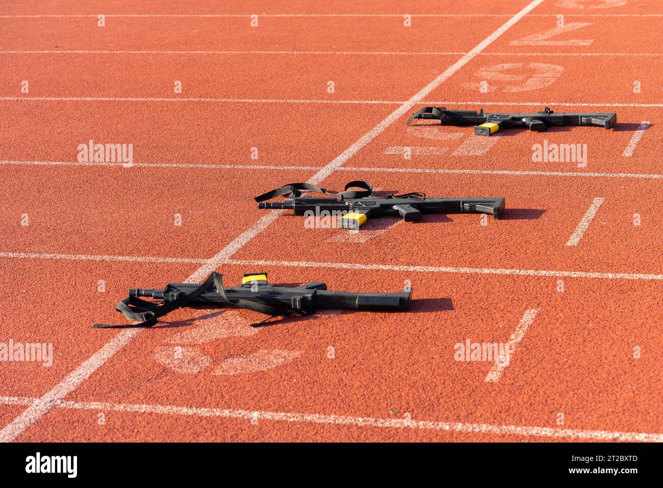 Black practice weapons on the dotted starting line of an orange running ...