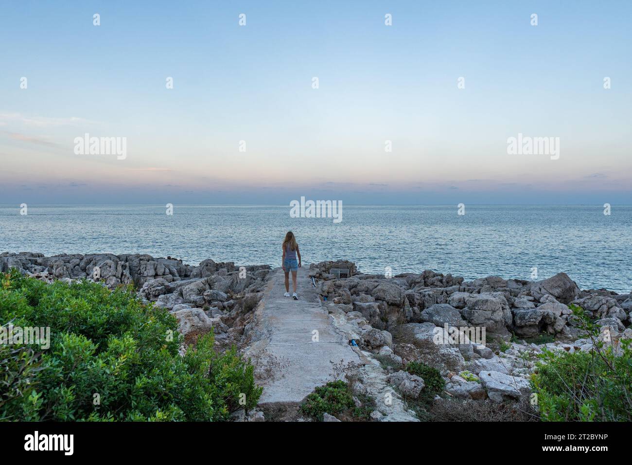 A blond girl walking on the stunning cliffs of Cala Ratjada watching ...