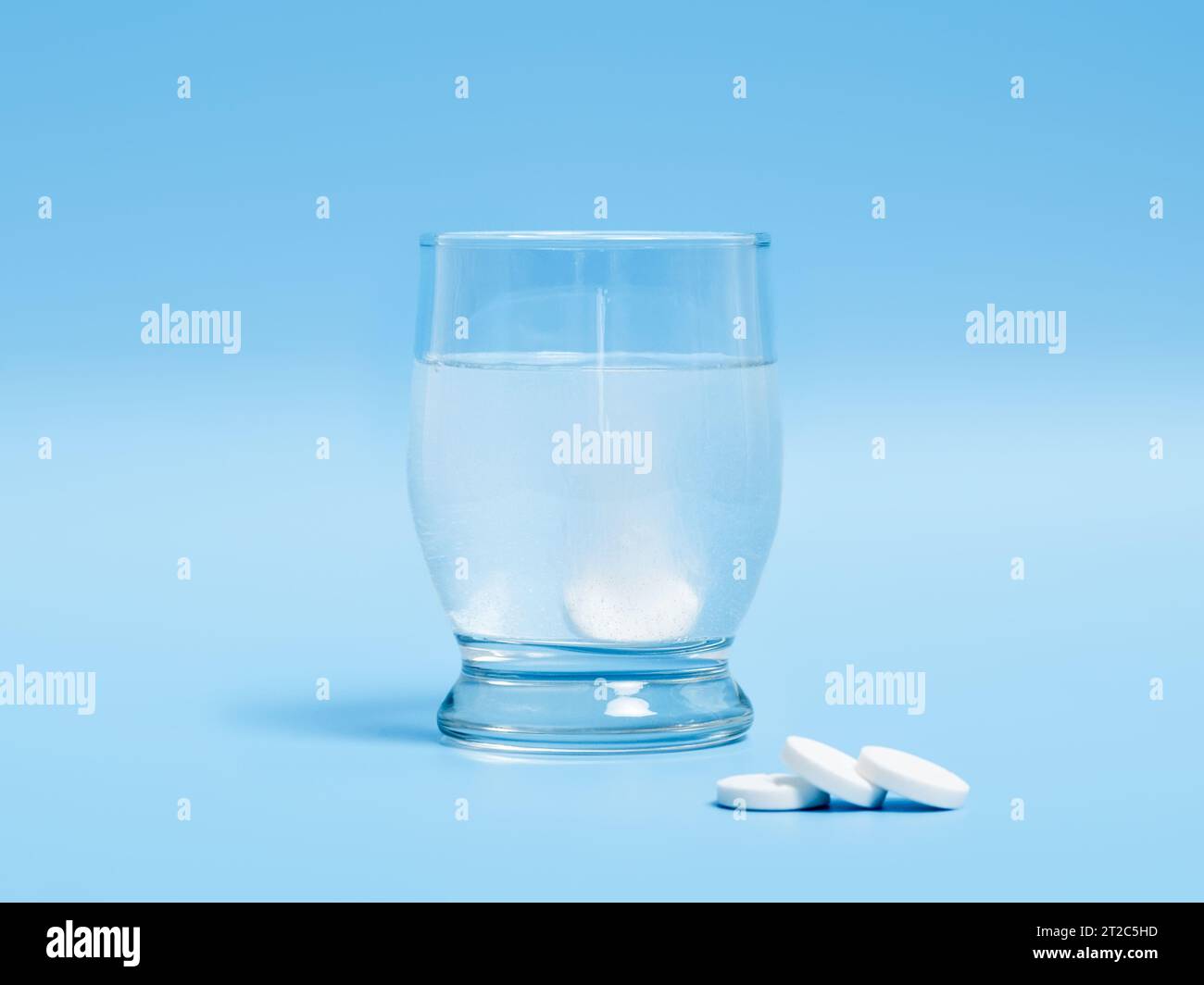 White effervescent tablet or vitamin C dissolving in glass of water on blue background ...