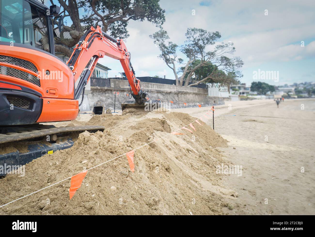 Bulldozer digging sand on a sandy beach. Unrecognizable people walking ...