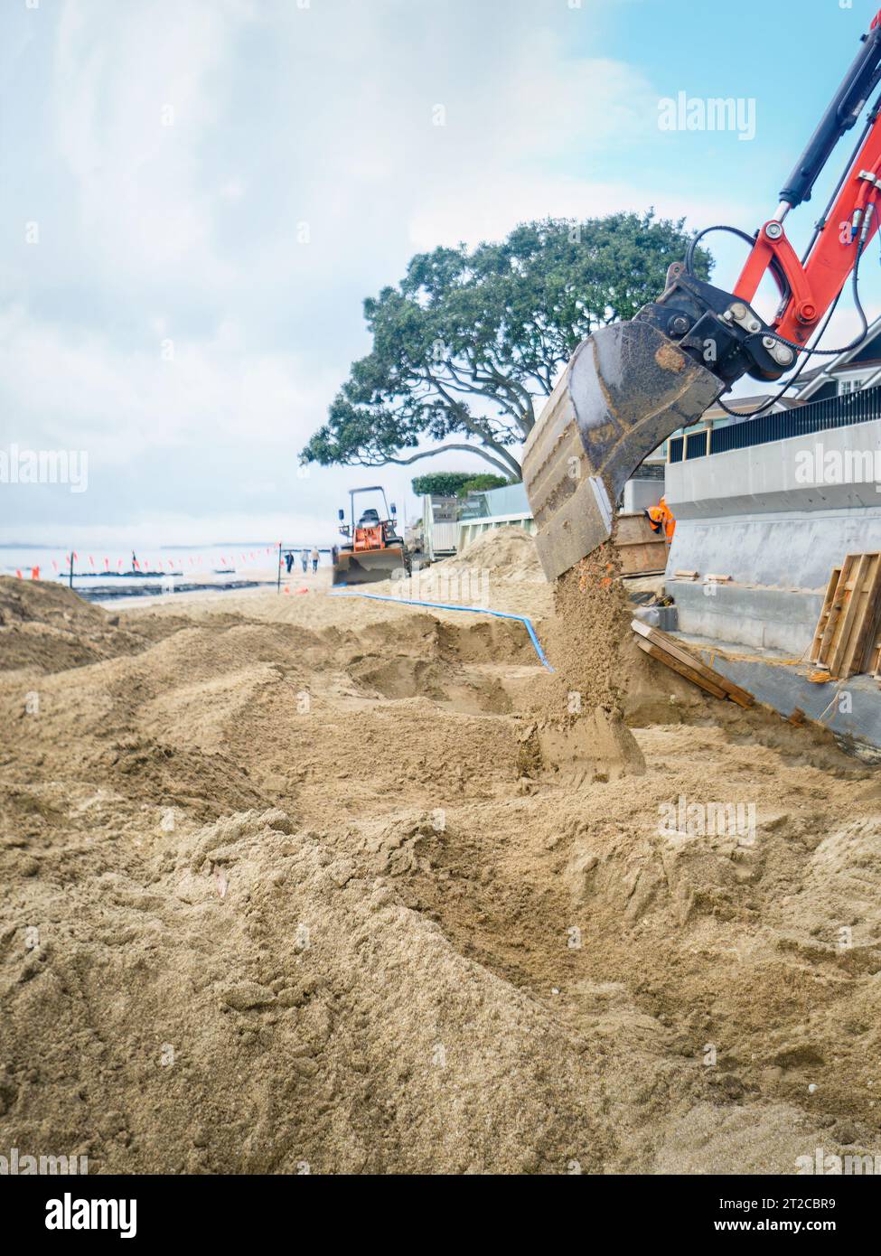 Bulldozer digging sand on a sandy beach. Houses and concrete retaining ...