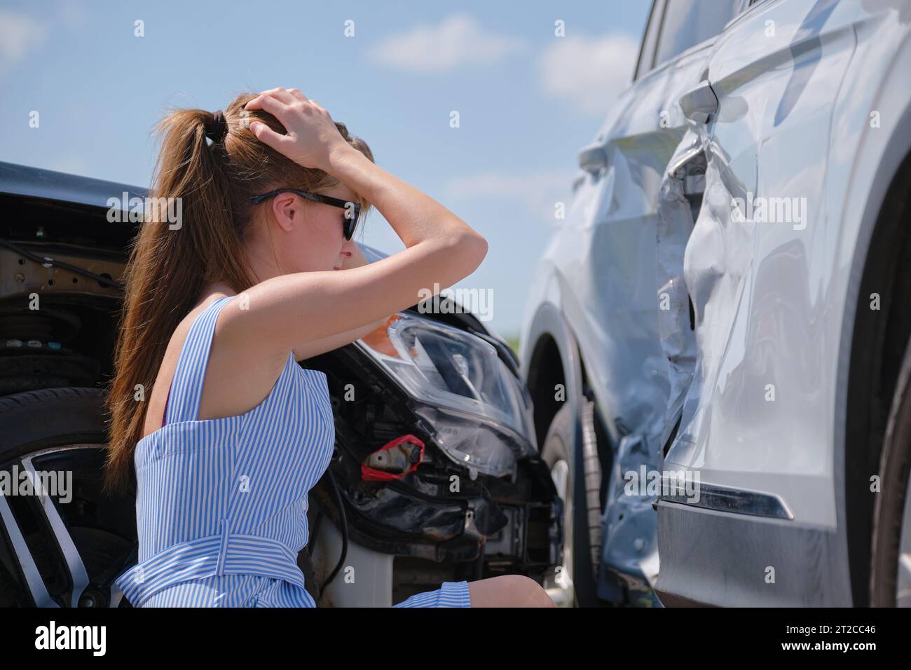 Sad young woman driver sitting near her smashed car looking shocked on ...