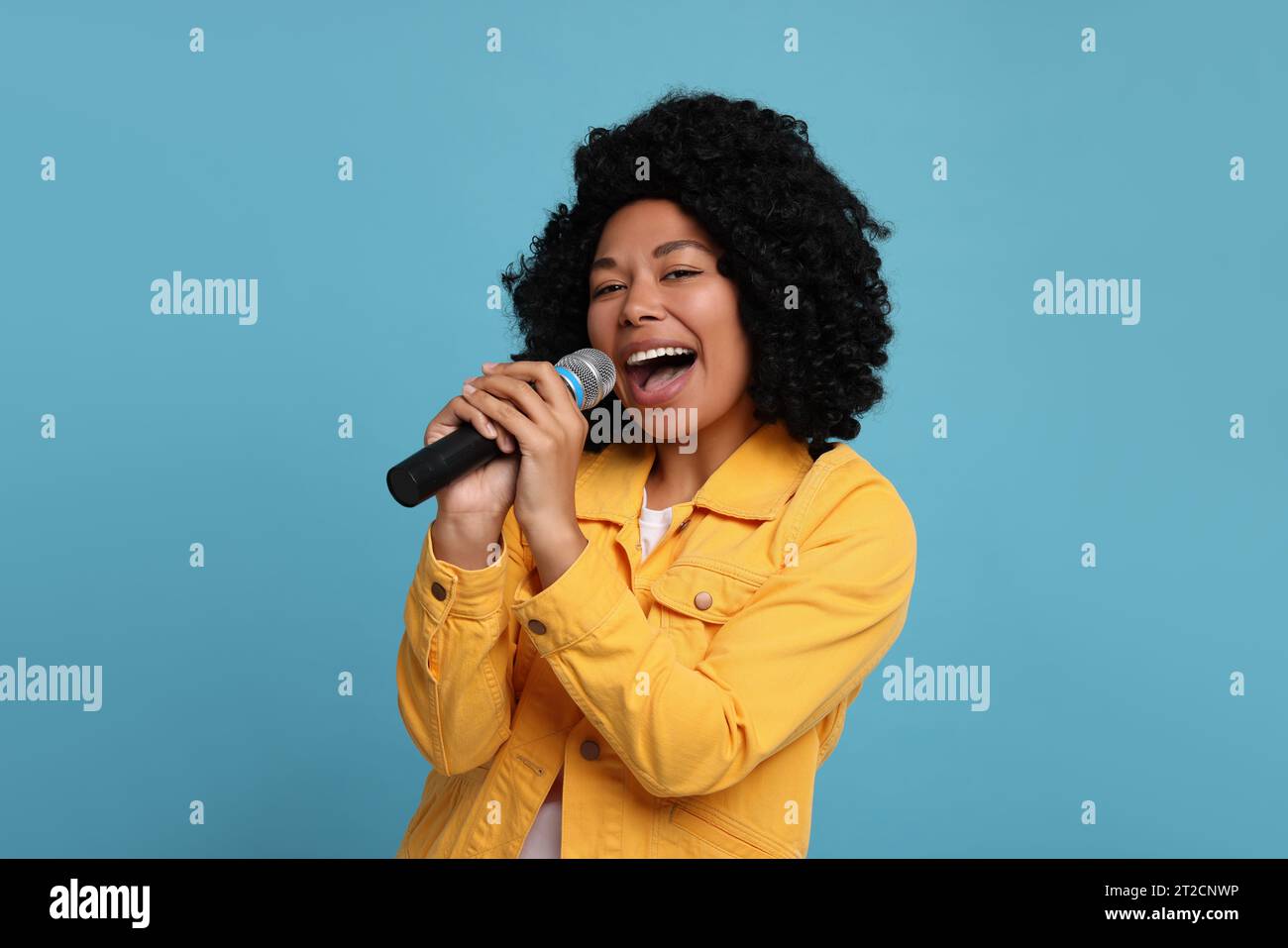 Beautiful woman with microphone singing on light blue background Stock ...