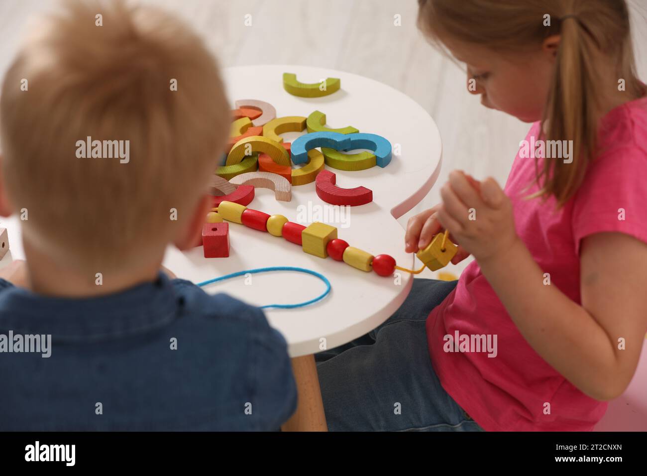 Little children playing with wooden pieces and string for threading ...