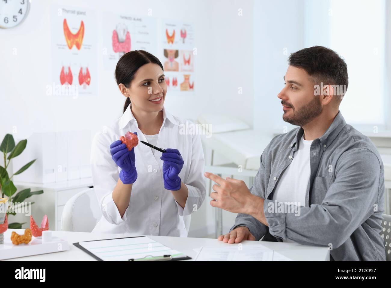 Endocrinologist showing thyroid gland model to patient at table in ...