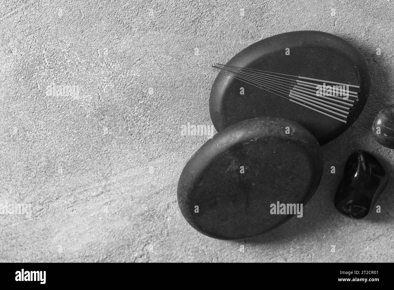 Stones with acupuncture needles on grey textured table, top view. Space ...