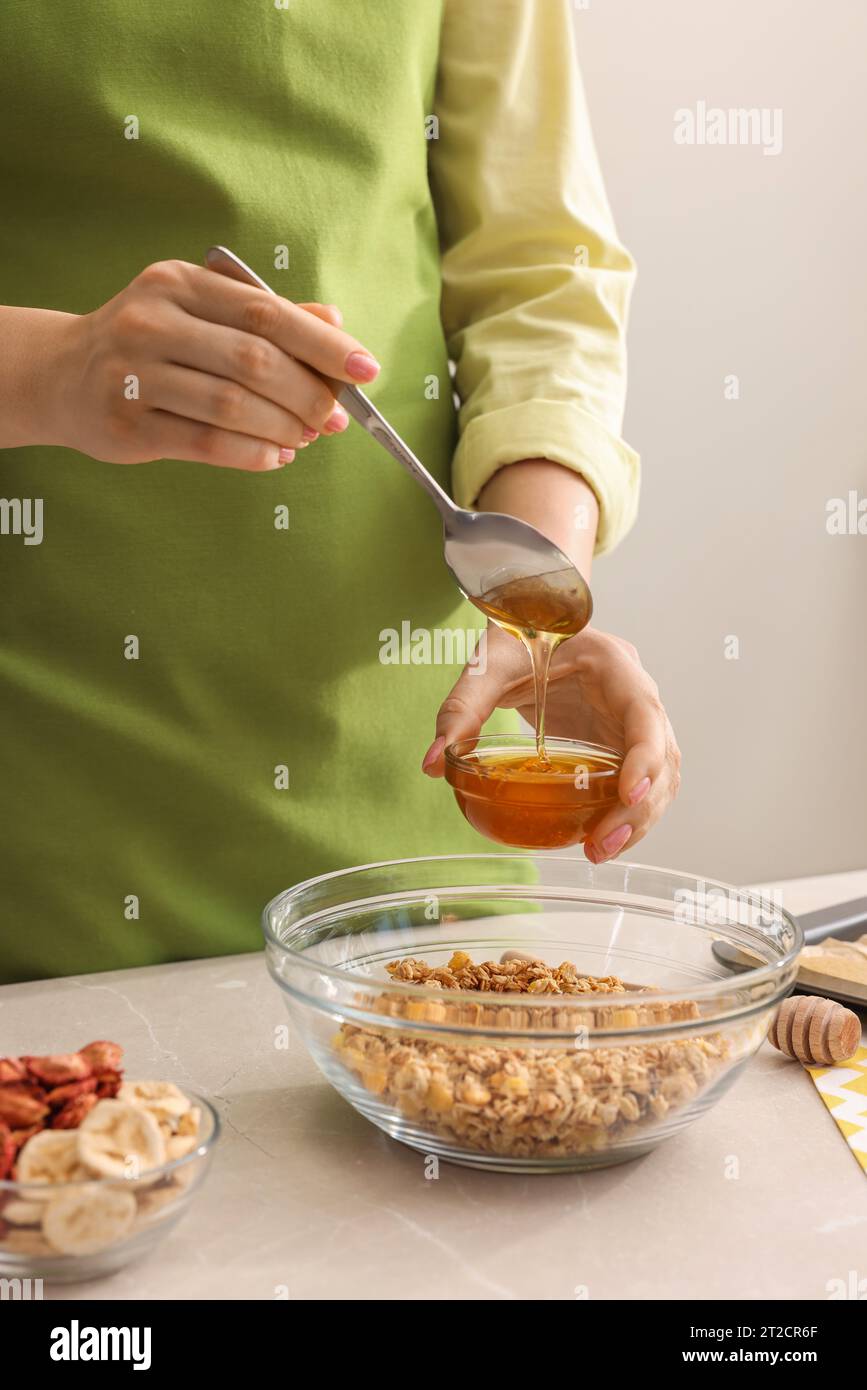 Making granola. Woman adding honey into bowl with mixture of oat flakes ...