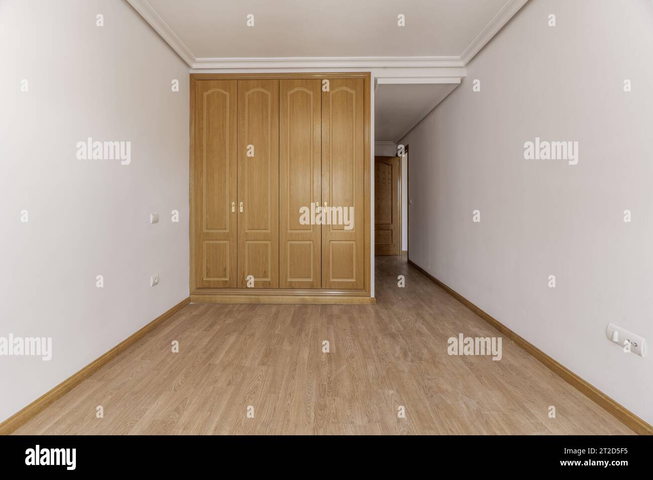 Empty bedroom with a built-in three-door oak wardrobe with gold handles ...