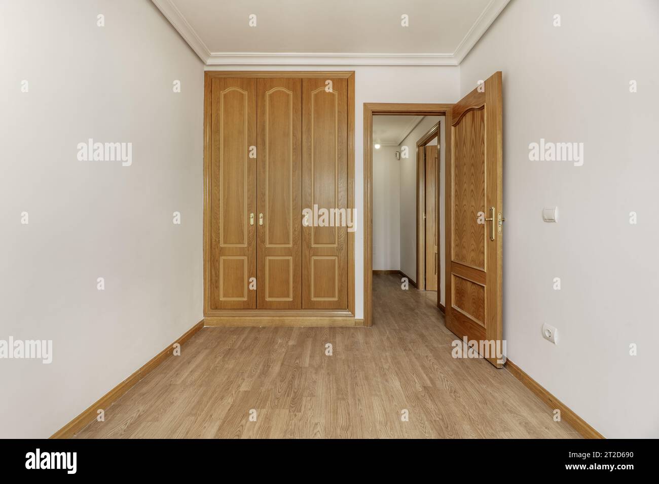 Empty bedroom with a built-in three-door oak wardrobe with handles, a ...