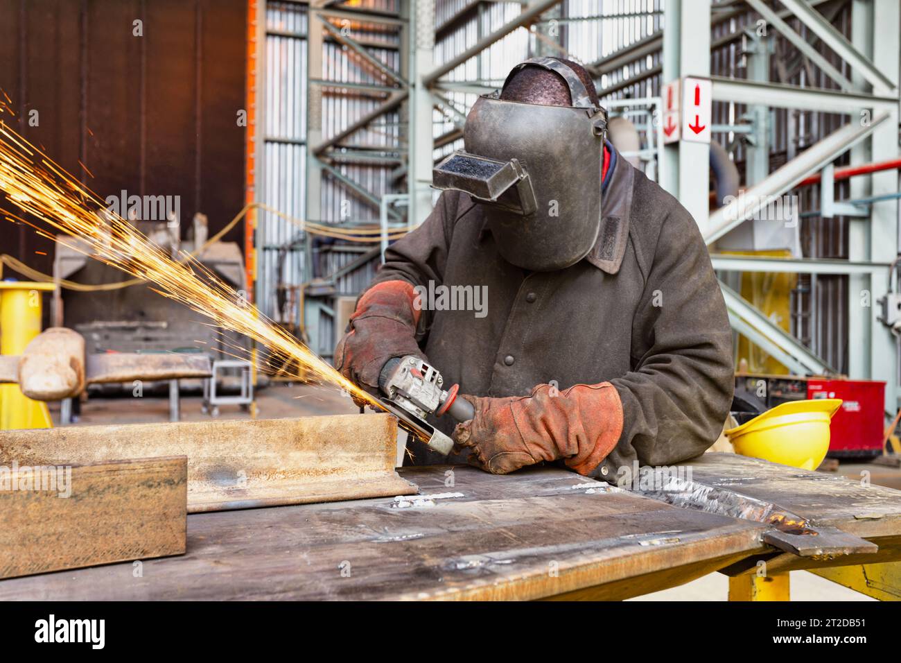 african man in the factory wearing a mask and working with a grinder ...