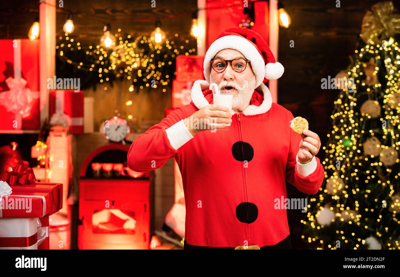 Happy Santa Claus eating a cookie and drinking glass of milk at home ...