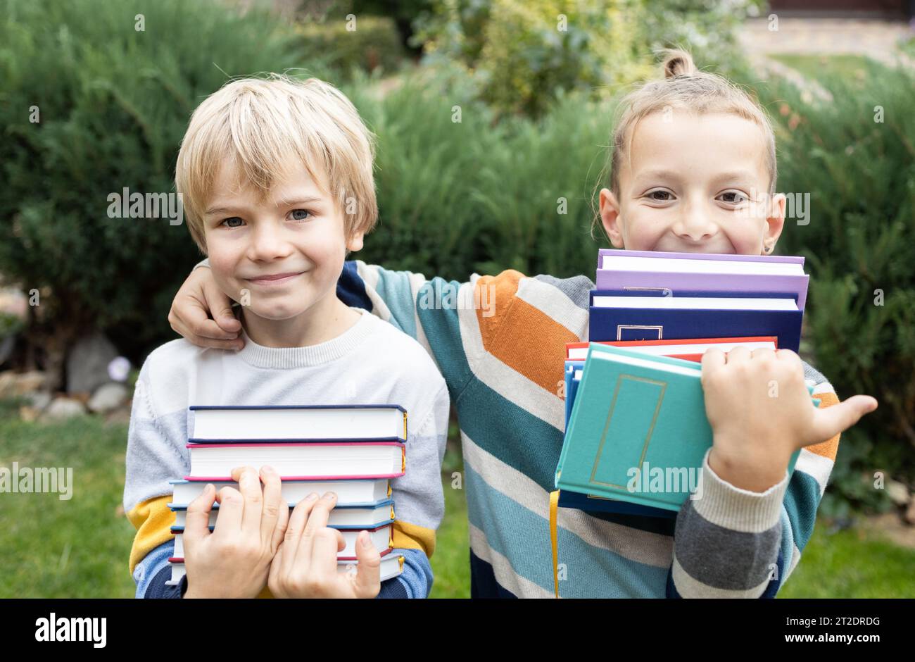Two boy friends stand next to each other and hold stacks of books in ...