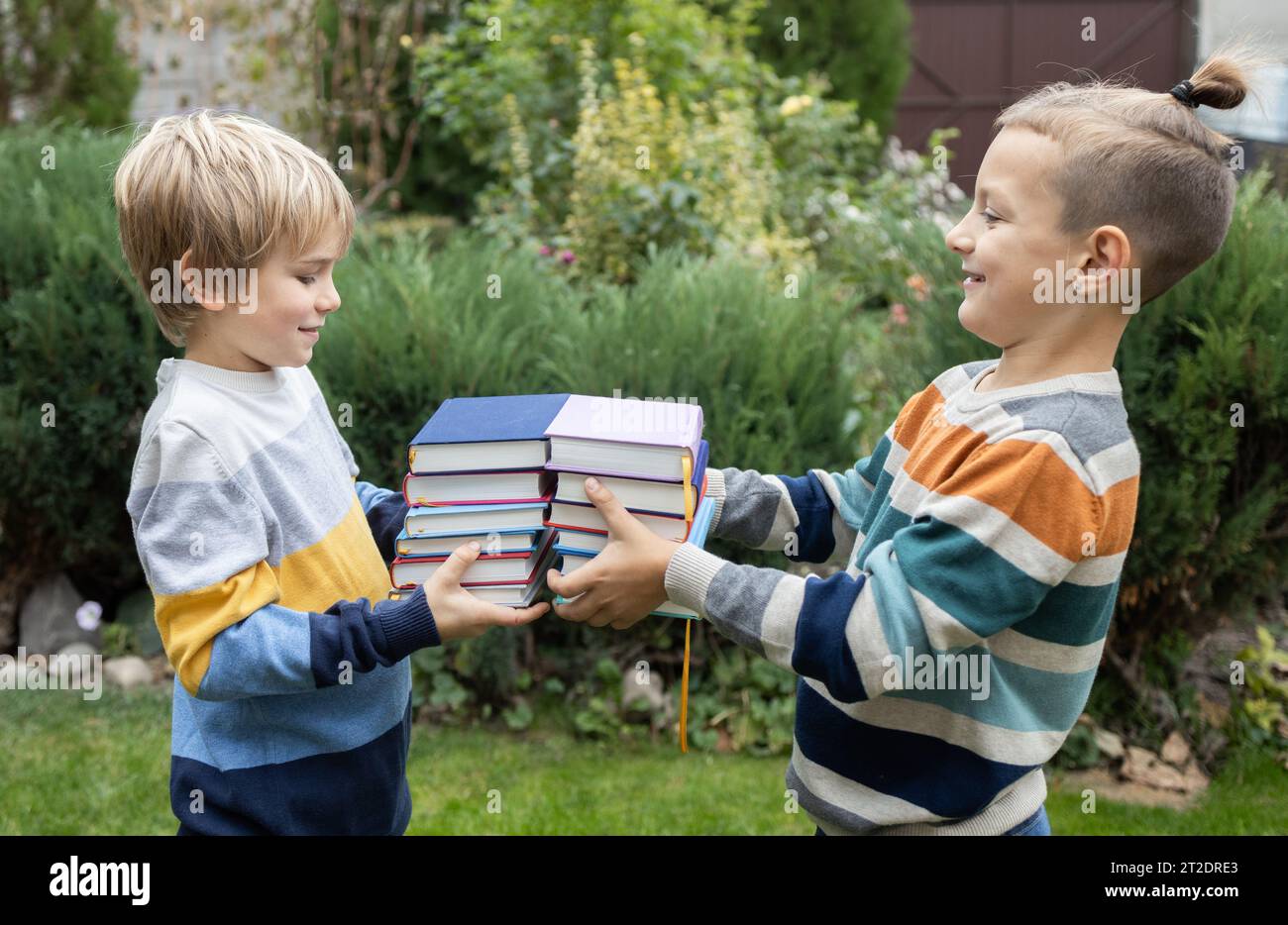 Two boy friends stand opposite each other and hold stacks of books in ...