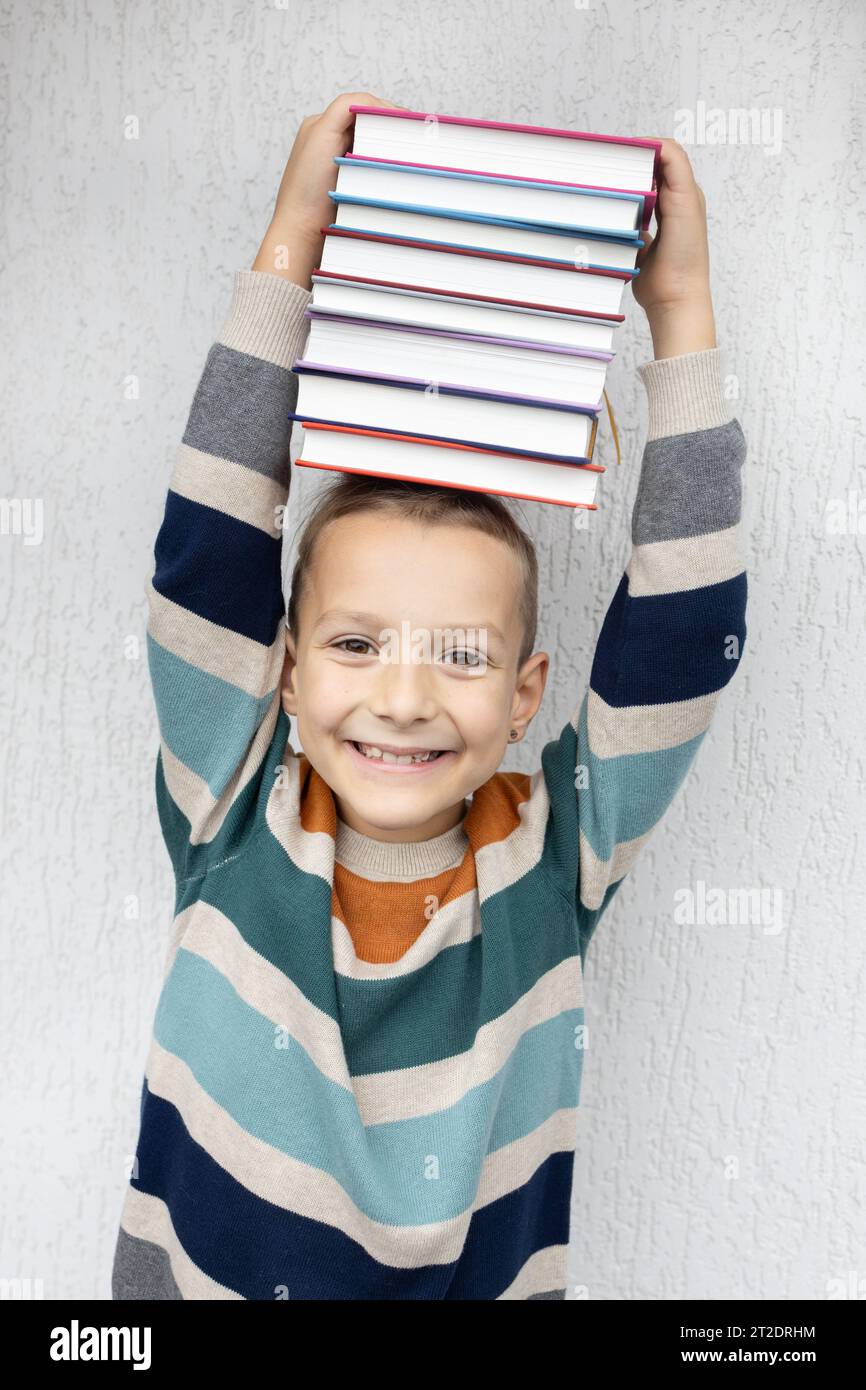 cheerful cute boy of 8 years old holds a stack of books on his head ...