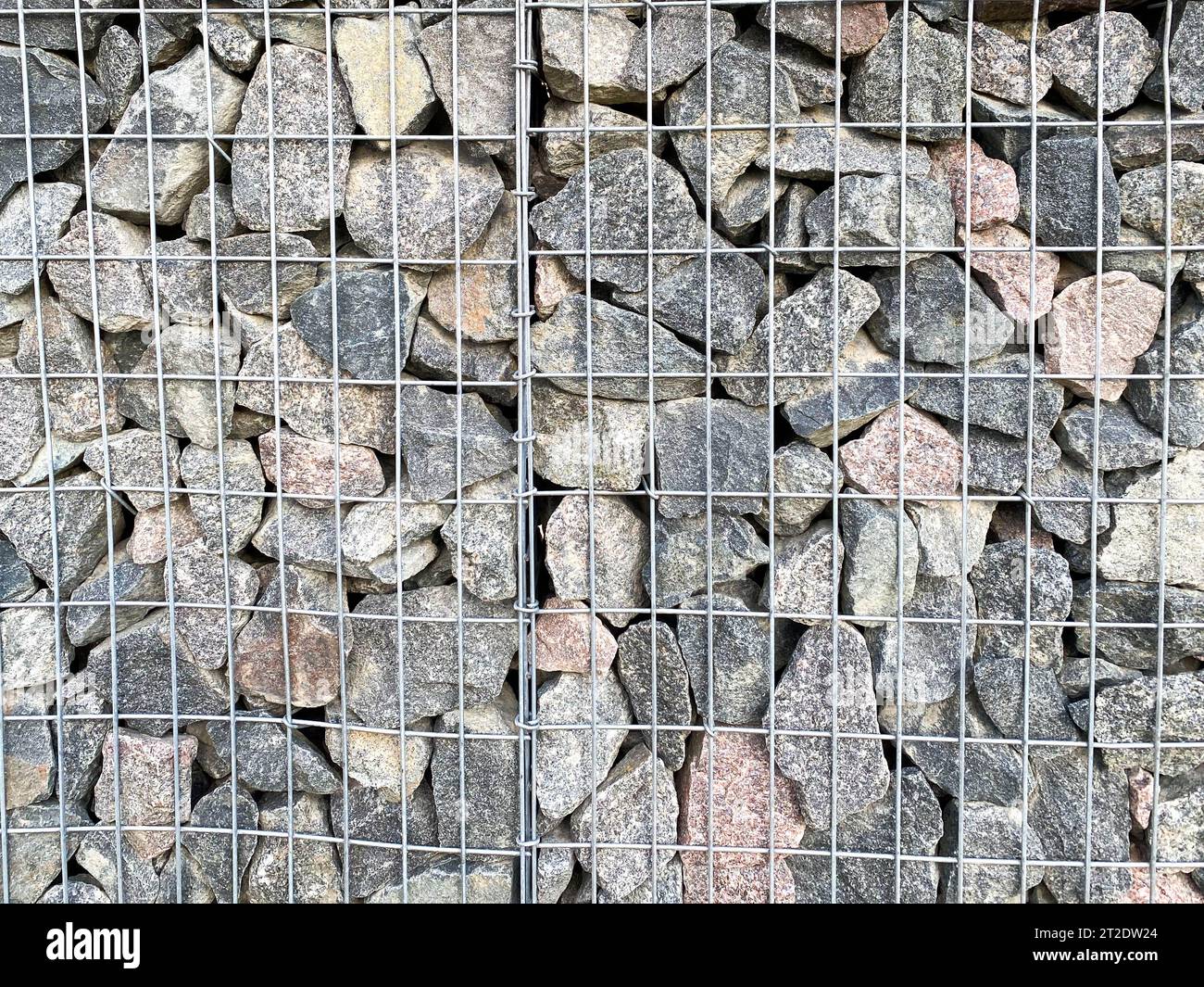Texture of metal wire mesh and large stones cobblestones inside. The ...