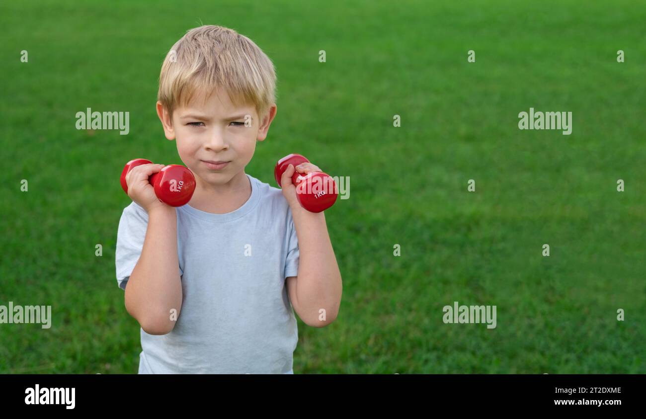 Sporty little boy lifting dumbbells on a green lawn. Joyful toddler ...