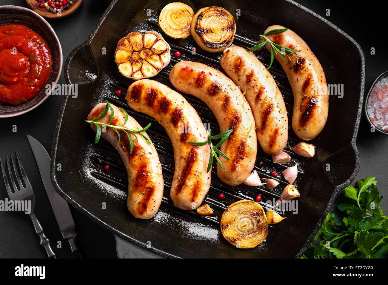 Grilled sausages with tomato sauce, vegetables and herbs on black cast ...
