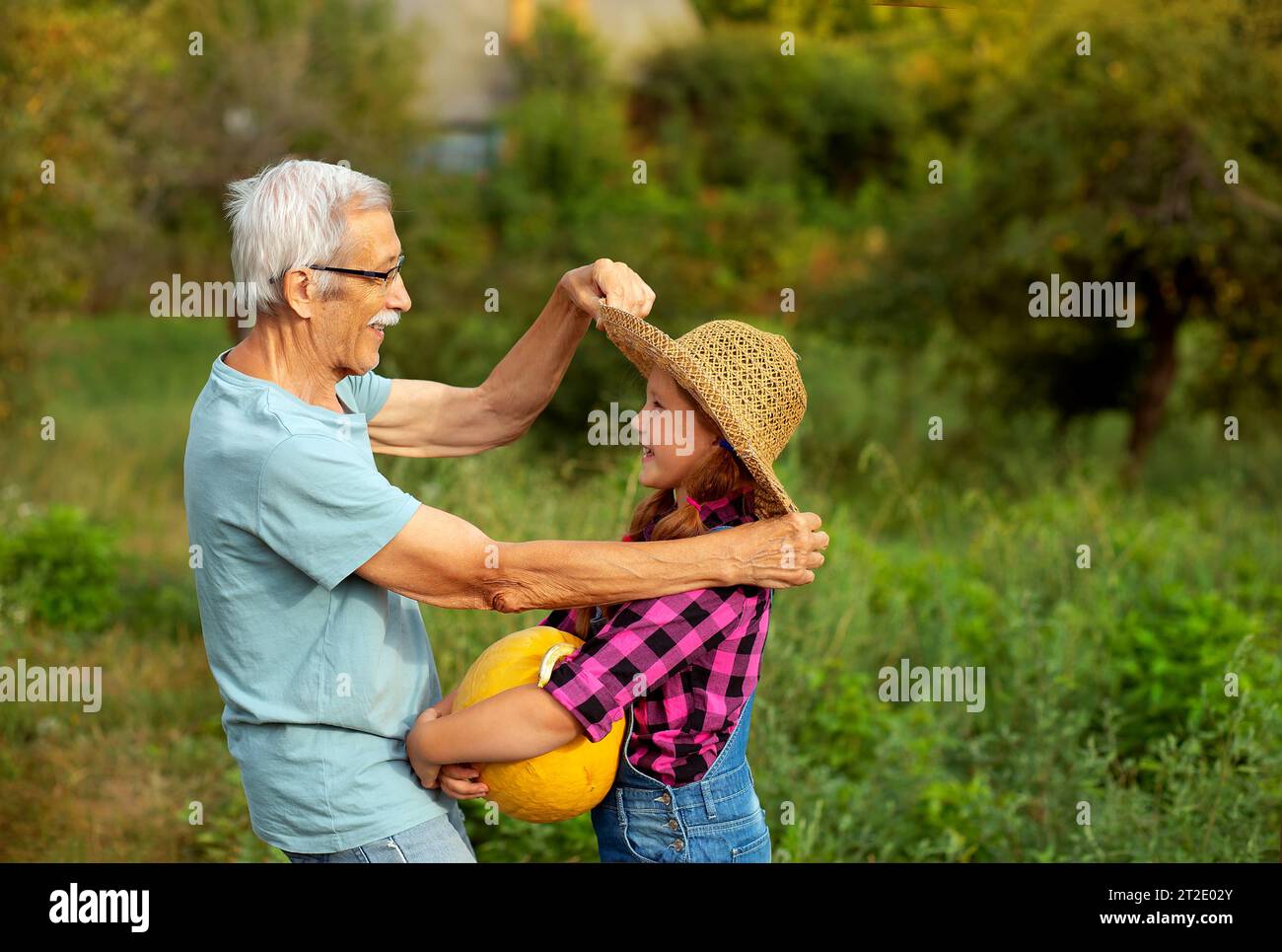 Happy cheerful old farmer grandfather puts his straw hat on his ...