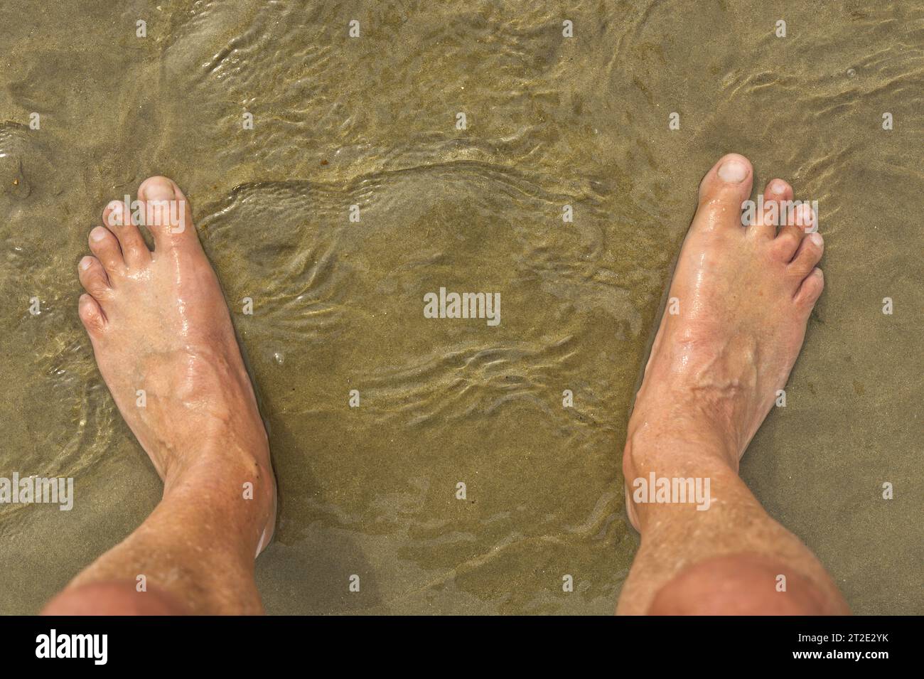 Pair of adult male feet on sandy beach with clear water. Looking ...