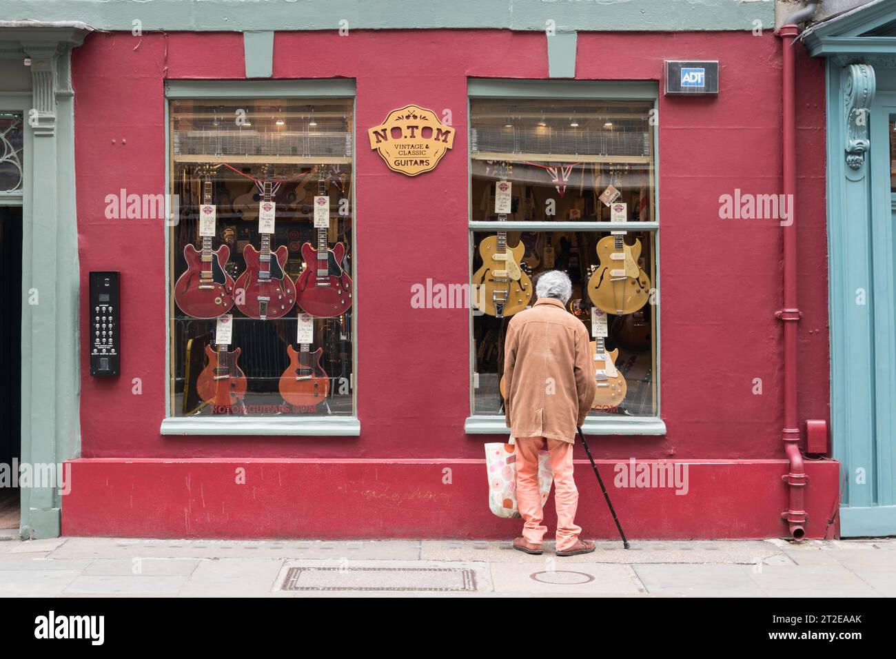 An elderly man with a walking stick window shopping at No. Tom Guitars, Denmark Street, London ...