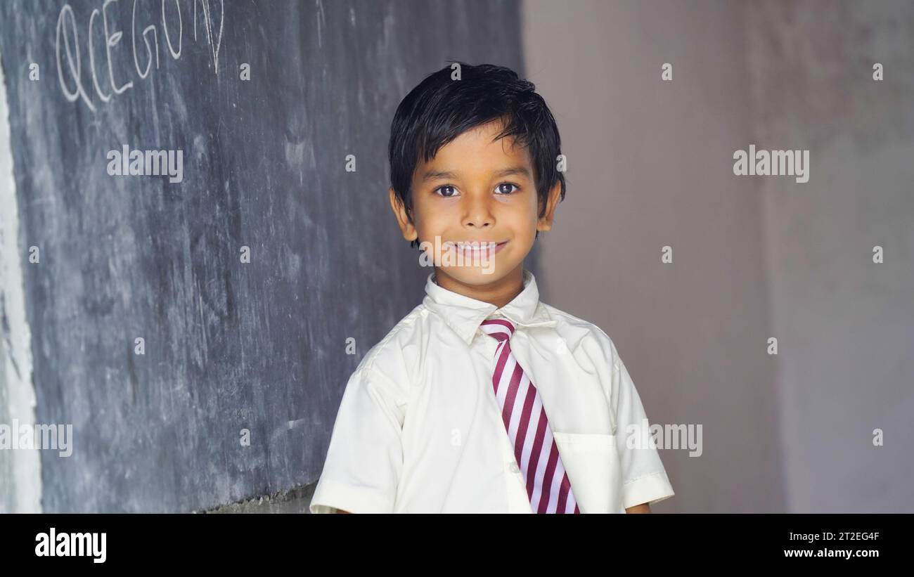 Indian school boy standing against blank chalkboard, intelligent and ...