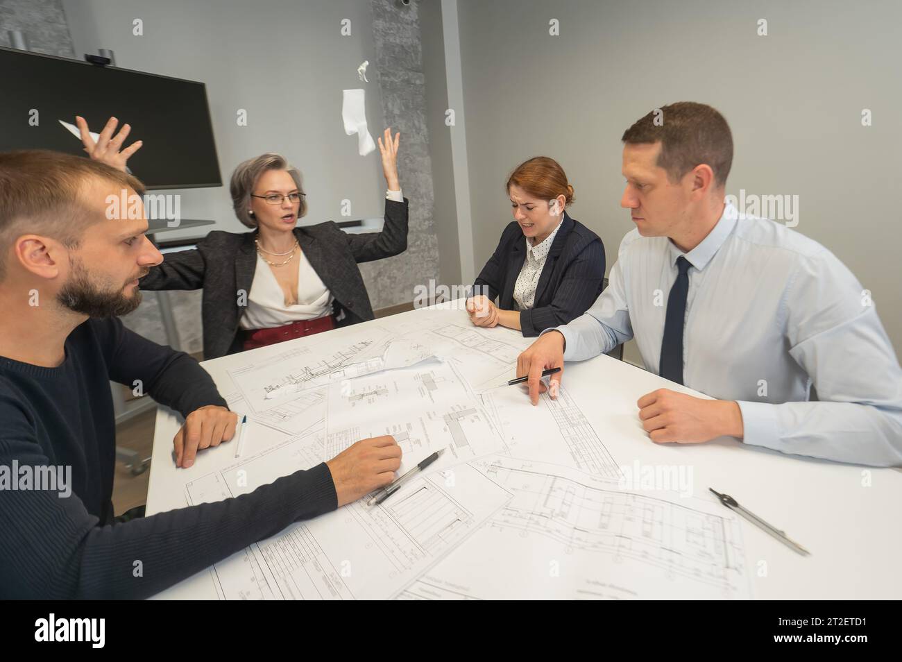 Four business people sitting around a table discussing blueprints ...