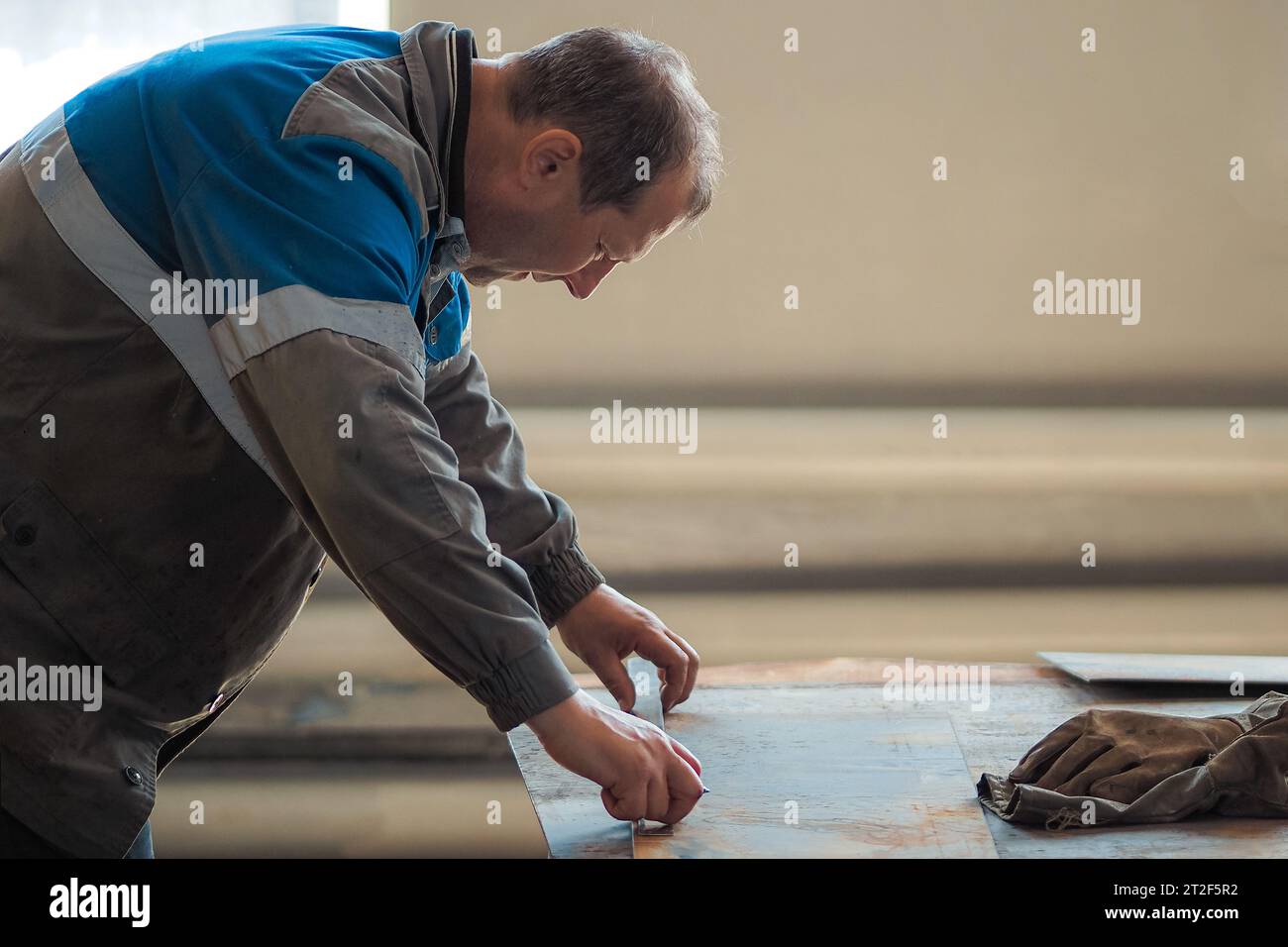 Working man works at workbench in workshop. Man in overalls measures ...