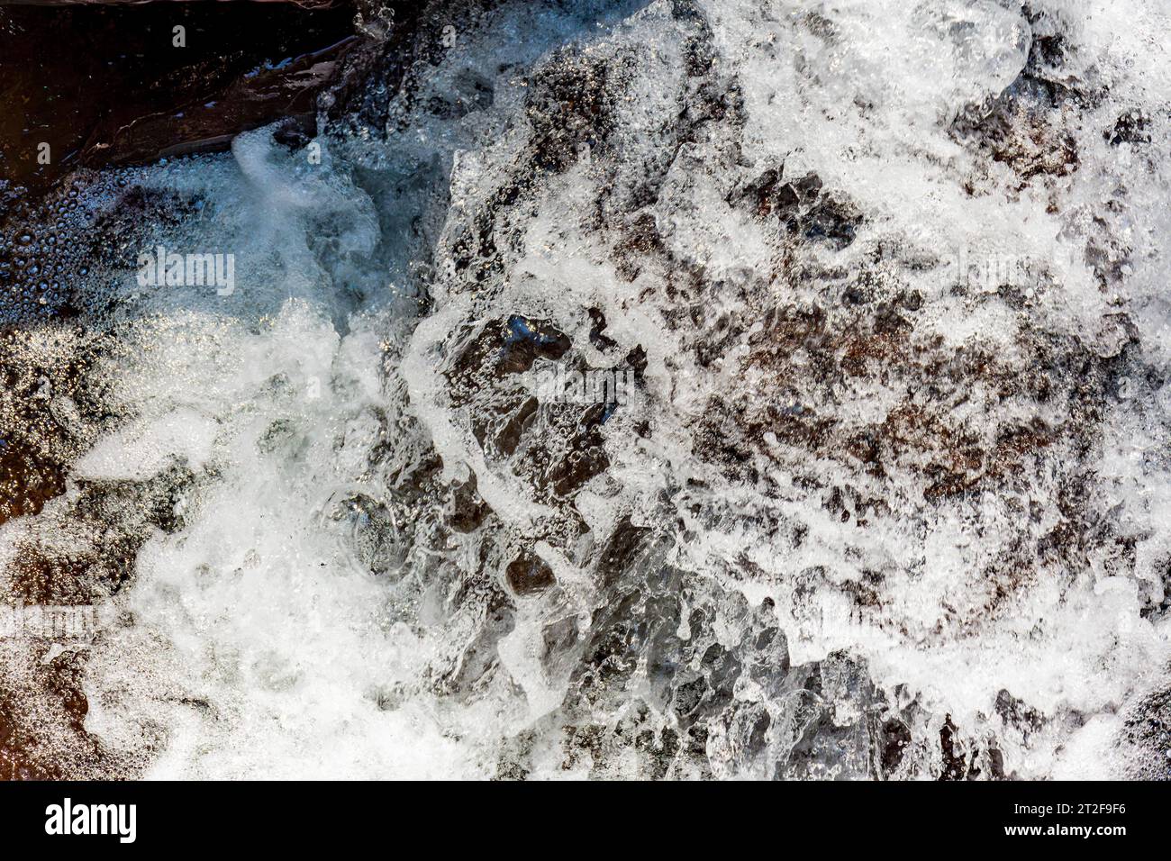 Texture of river water with foam and bubbles running between the stones ...