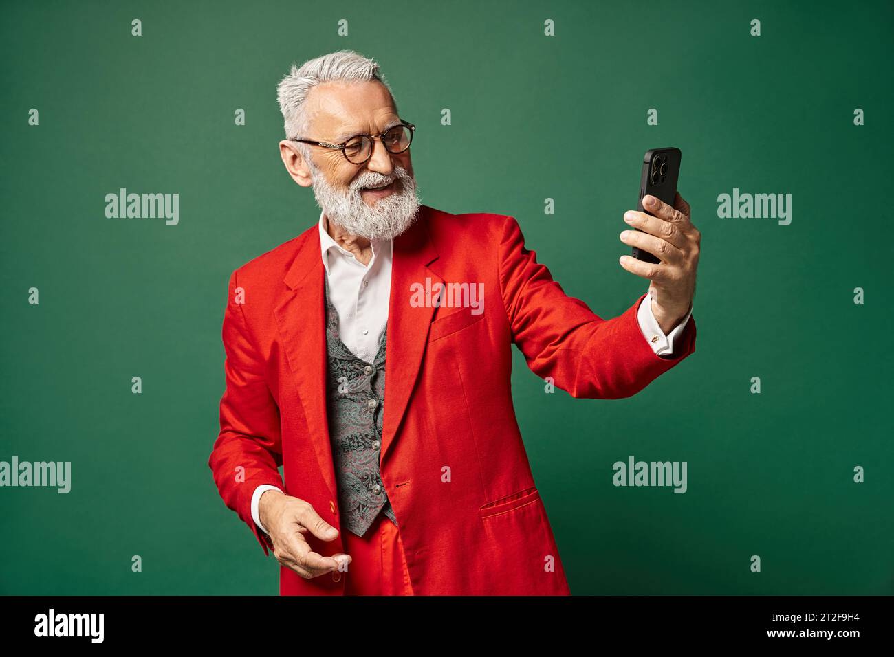elegant good looking Santa in classy red attire taking selfie on green ...