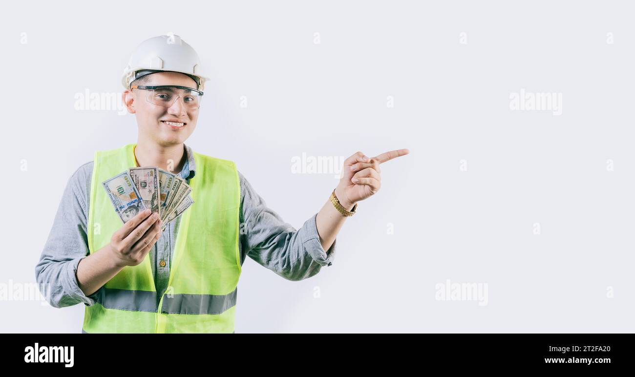 Smiling young engineer holding money pointing aside isolated. Handsome ...