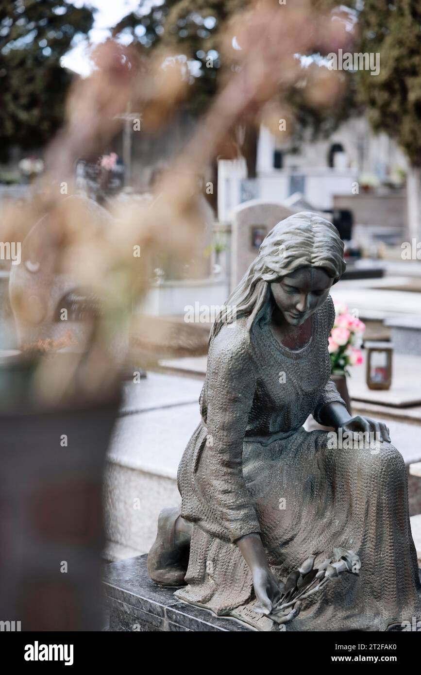 Statue of a mourning woman laying flowers on a grave in a cemetery ...