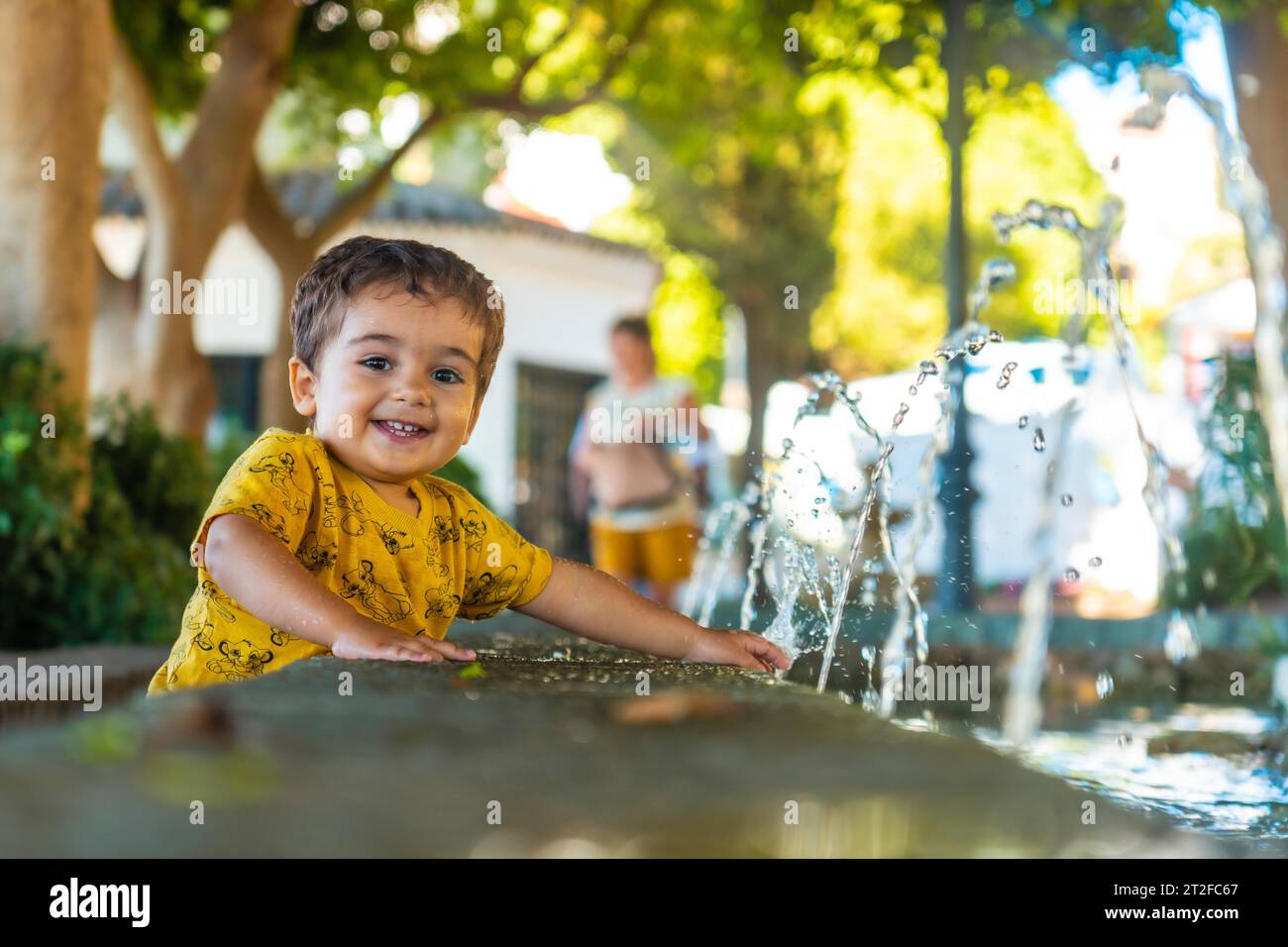 A smiling baby cooling off from the heat in the fountain in the ...